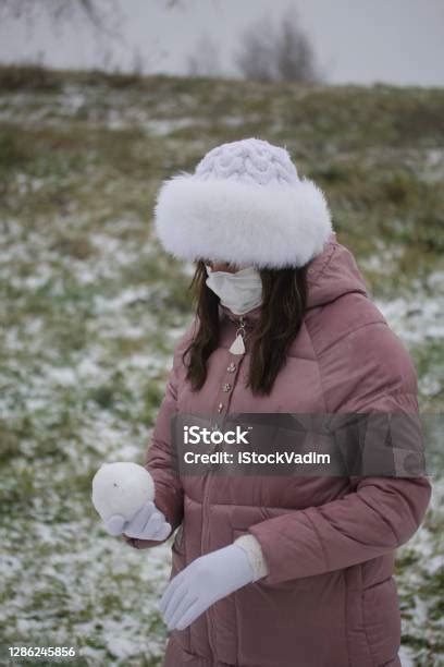 공원에서 산책에 의료 마스크와 겨울 옷을 입은 소녀 그의 손에 눈의 공을 들고 땅은 첫 번째 눈으로 덮여있다 35 39세에 대한 스톡 사진 및 기타 이미지 Istock