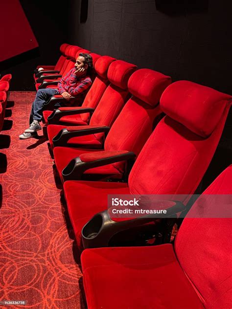 영화를 보기 위해 벨벳 영화관 좌석에 앉아 있는 인도 남자의 이미지 팝콘 욕조 음료 홀더가 있는 계층화된 빨간색 좌석 행 프로필 보기 전경에 초점 영화관에 대한 스톡 사진