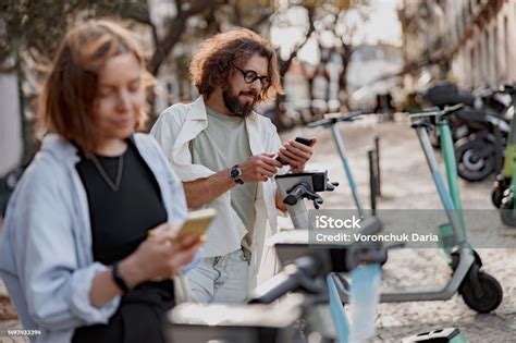 부부는 도시의 거리에 서서 휴대 전화를 사용하여 전기 푸시 스쿠터를 대여합니다 2명에 대한 스톡 사진 및 기타 이미지 2명