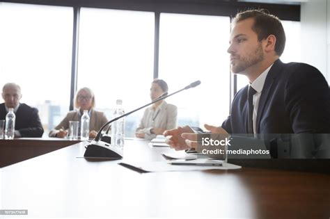 벌 나무 테이블에 앉아 및 개발의 계획 회의에서 기자 들과 공유 하는 동안 마이크에 말하기에 심각한 자신감 잘생긴 젊은 사업가 경영자에 대한 스톡 사진 및 기타 이미지