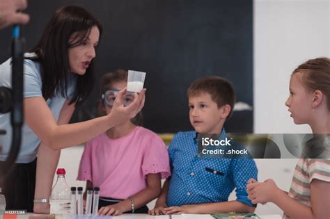 초등학교 과학 교실 열정적 인 교사는 비커에서 화학 물질을 혼합하는 어린이의 다양한 그룹에 화학을 설명합니다 아이들은 관심으로