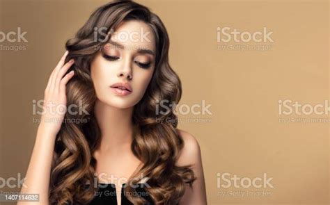 젊고 갈색 머리의 아름다운 모델은 길고 곱슬곱슬하고 잘 손질 된 머리카락 헤어 케어 및 미용 예술 헤어 스타일리스트에 대한 스톡