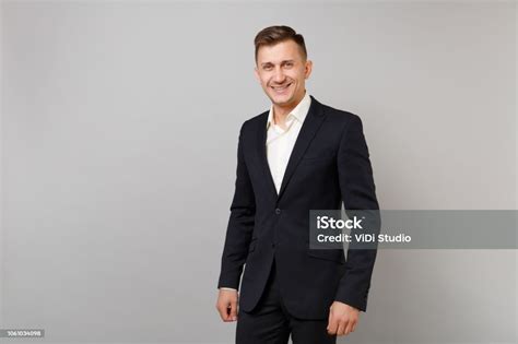 고전적인 검은 양복에 웃는 잘생긴 젊은 비즈니스 남자의 초상화 흰 셔츠 서 스튜디오에 회색 벽 배경에 고립 성과 경력 부 비즈니스 개념입니다 복사 공간을 비웃는 다 검은색에