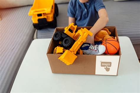 접힌 옷과 장난감으로 가득 찬 골판지 기부 상자를 들고있는 사랑스러운 소년 2022년에 대한 스톡 사진 및 기타 이미지