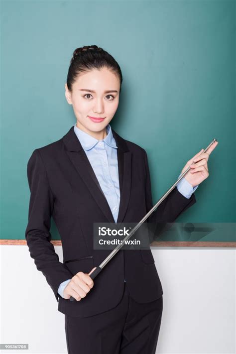Portrait Of Female Teacher Holding Pointer Stick Front Of Blackboard