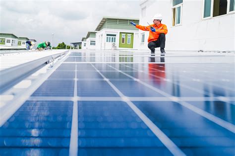 주황색 안전조끼를 입은 작업자가 노트북을 사용하여 옥상의 태양 전지판을 검사하고 적절한 유지 관리를 확인합니다 이 장면은 재생 에너지 태양열 기술 및 지속 가능한 관행을