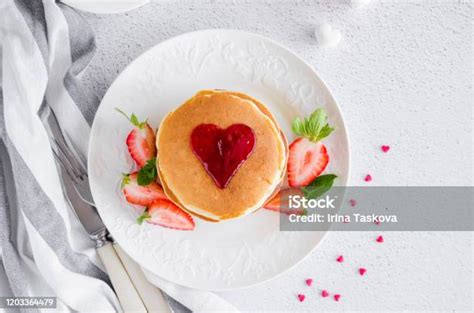 신선한 딸기와 민트가 밝은 배경의 흰색 접시위에 잼의 심장이 있는 팬케이크 더미 발렌타인 데이 아침 식사 수평 방향 공간을