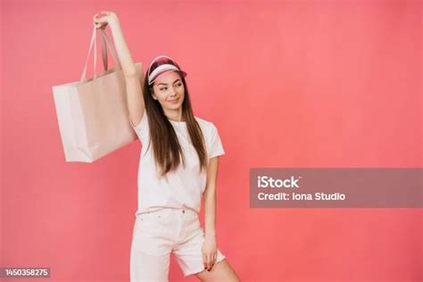 흰색 티셔츠에 긴 머리를 가진 젊은 이탈리아 여성 컬러 투명 바이저 쇼핑백을 올리고 복사 공간을 옆으로 바라보고 쇼핑 후 행복
