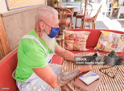 바에 앉아 스마트 폰과 힙스터 남자 노인은 기술을 즐길 수 있으며 보호 얼굴 마스크를 착용 코론 바이러스 라이프 스타일 60 69세에 대한 스톡 사진 및 기타 이미지