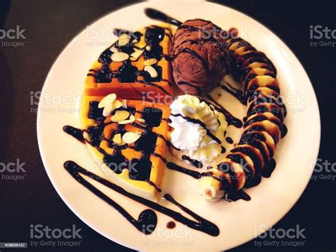 음식과 디저트 개념입니다 초콜릿 아이스크림 화이트 크림 와플 바나나를 슬라이스 하 고 액체 초콜릿 슬라이스 아몬드를 얹은 흰색 접시에 있다입니다 포그라운드에 초점 갈색에