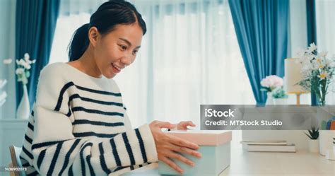 흥분한 젊은 아시아 소녀는 책상 위에서 행복한 순간과 함께 유리 가게에서 선물 오프닝 언 박스 민트 핑크 파스텔 박스 선물을받는 스웨터를 착용합니다 개봉에 대한 스톡 사진