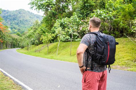 태국 숲으로 가는 길에 배낭을 메고 여행자 청년과 함께 잘 생긴 열대 우림 한 남자가 열대 도로를 걷고 자연의 전망을 즐깁니다 감시에 대한 스톡 사진 및 기타 이미지