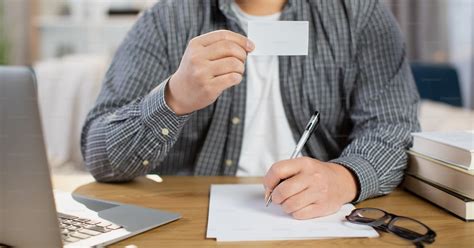 젊은 남자의 클로즈업은 무선 노트북으로 책상에 앉아 빈 흰색 카드를 보여주는 캐주얼 복장을 얻습니다 명함에 텍스트를 넣을 공간입니다 사진 Unsplash의 종이 이미지