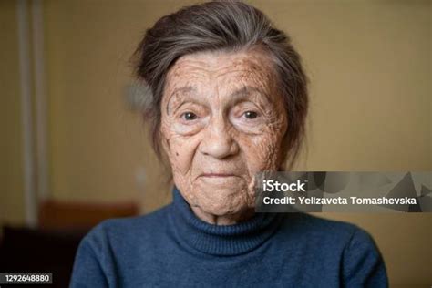 회색 머리와 주름진 얼굴을 가진 90 세의 백인의 오래된 귀여운 여성은 카메라 귀여운 표정과 미소를 보입니다 성숙한 할머니는 긴 간 테마 감정과 노인의 기분을 은퇴 명랑한에