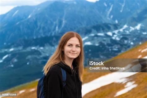 따뜻한 회색 스웨터를 입은 귀여운 금발 소녀가 산 꼭대기에 올라 사진작가의 카메라를 바라보고 있습니다 여행 일 개념입니다 관광 모험 개념에 대한 스톡 사진 및 기타 이미지