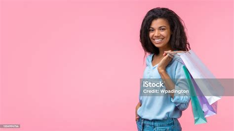 파스텔 핑크 배경에 고립 된 손에 종이 쇼핑 가방더미와 함께 포즈를 취하는 완벽한 미소와 매력적인 세련된 아프리카 소녀의 초상화 가방에 대한 스톡 사진 및 기타 이미지