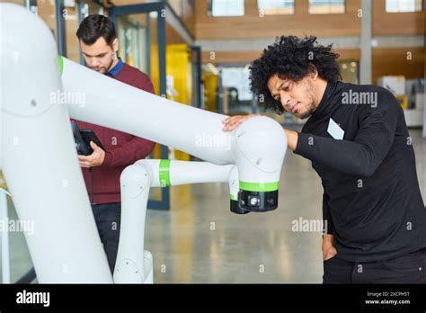 Two Engineers Programming And Inspecting A Robotic Gripper Arm Emphasizing Industrial
