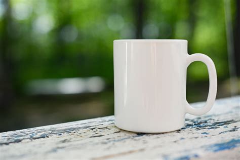 하얀 머그잔 모형 녹색 배경에 흰 머그잔 커피 차 아침 아침 식사 애프터눈 티 캠핑 피크닉 음료 글쓰기를위한 장소가있는 머그잔 야외에서 흐릿한 배경 정원의 차 머그에 대한