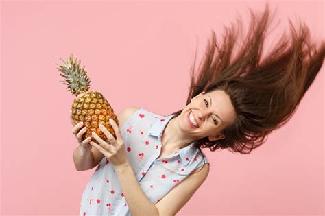 분홍색 파스텔 벽 배경에 고립 된 신선한 잘 익은 파인애플 과일을 잡고 머리를 끼고 여름 옷을 입고 웃는 젊은 여자 사람들은 생생한 라이프 스타일 휴식 휴가 개념입니다 복사