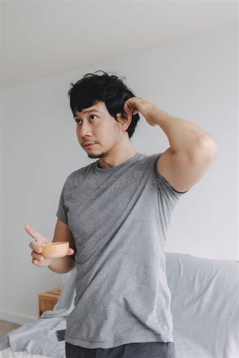 Man Scratching His Head Standing In The Room And Holding A Cup Of Peanuts Stock Photo Image