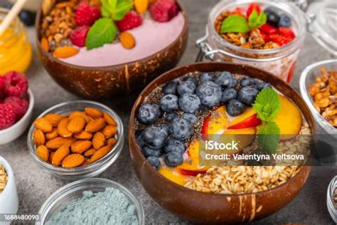 요구르트와 신선한 아몬드 블루베리 라즈베리 복숭아 딸기를 식탁에 올려놓은 그래놀라 그릇 아사이와 스피루리나 그릇 건강한 아침 식사 Conceptcopy 공간 텍스트를 위한