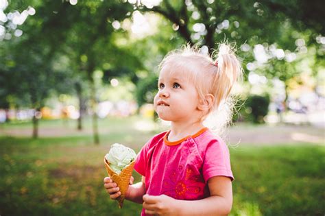 재미 있은 소녀 금발에 공원에서 녹색 여름 배경 와플 컵에 먹는 달콤한 블루 아이스크림 그녀의 얼굴 및 뺨과 웃음을 발 랐 습 밝고 세련 된 옷을 입고 감탄에 대한 스톡