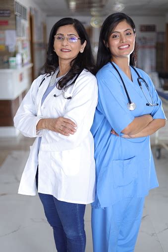 등을 맞대고 서 있는 인도 여성 의사의 전체 길이 프로필 사진 흰 양복을 입은 선배 의사와 파란 제복을 입은 간호사 간호조무사에 대한 스톡 사진 및 기타 이미지 Istock