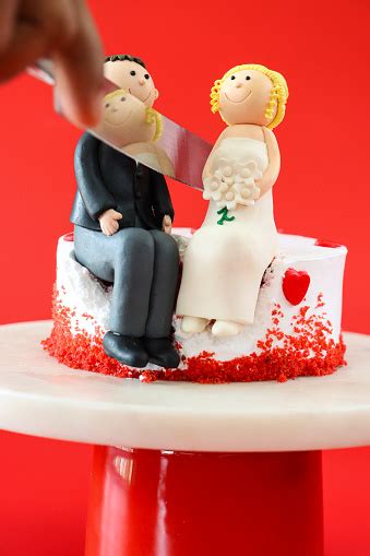 신부와 신랑 토퍼가 각각을 바라보며 앉아있는 클로즈업 이미지 빨간 퐁당 아이싱 하트로 덮인 흰색 아이스 웨딩 케이크 층으로 자르고 빨간 바탕 빨간 배경 전경에 초점을 맞춘