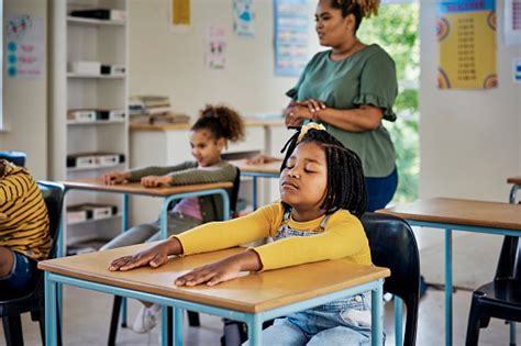 교사 교실 및 학교에서 학습 교육 또는 아동 발달을 위한 명상을 하는 어린이 어린 흑인 여학생이 수업 중 듣기 테스트 차분한 활동 또는 치료를 위해 책상에 앉아 있습니다