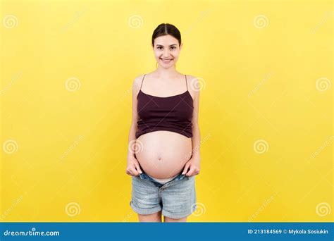 Happy Pregnant Woman In Unzipped Jeans Showing Her Belly At Colorful