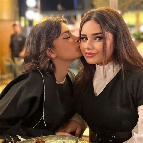 Two Women Are Kissing Each Other While Sitting At A Table In Front Of A Plate