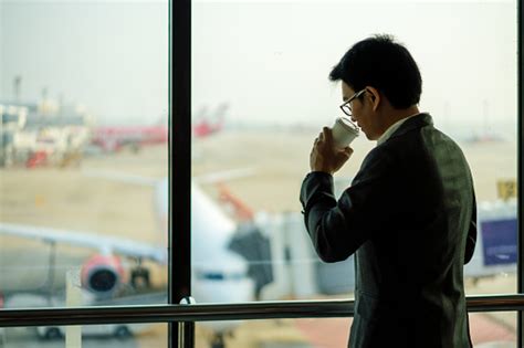 양복과 젊은 아시아 사업가 국제 공항에서 대기실에 스마트폰 사용 하는 동안 뜨거운 커피 한 잔을 누르고 비행기를 보고 서 공항에 대한 스톡 사진 및 기타 이미지 Istock