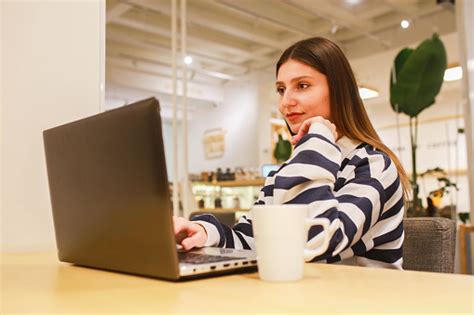 갈색 머리를 가진 젊은 아름다운 여자가 카페에서 커피를 마시고 노트북으로 원격으로 하이브리드 방식으로 고객과 이야기합니다 25