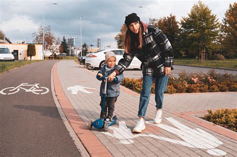 다른 아들과 아들이 재미 있습니다 행복한 가족 어머니는 아이 아들에게 도시 거리에서 스쿠터를 타도록 가르칩니다 어린 시절의 부모 역할 아이디어를 지원하십시오 행복한 가족