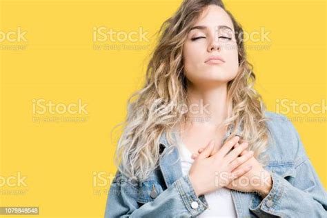 함께 웃 고 고립 된 배경 위에 데님 자 켓을 입고 아름 다운 젊은 금발의 여 자가 가슴 닫힌된 눈과 얼굴에 감사 제스처에 손 건강 개념입니다 감사에 대한 스톡 사진 및