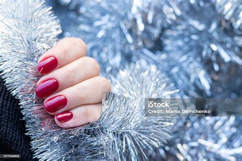 검은 니트 장갑 미트에 여성 손 아름다운 광택 매니큐어 부르고뉴 어두운 빨간색 체리 색상 손톱은 복사 공간과 실버 크리스마스 틴셀 화환의 배경에 손톱 갈란드 장식품에 대한