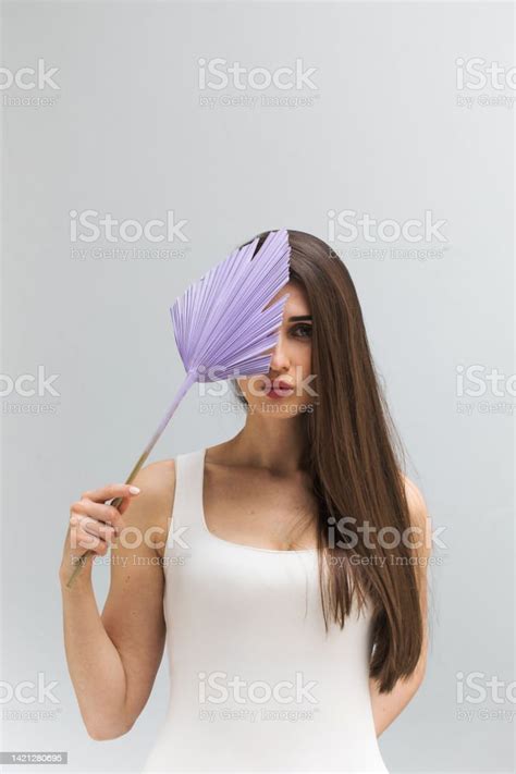 매력적인 갈색 머리 여자는 스튜디오에서 보라색 이국적인 식물 잎 뒤에 얼굴을 숨 깁니다 25 29세에 대한 스톡 사진 및 기타