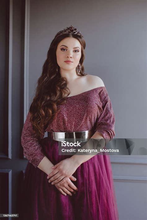 긴 보라색 여왕의 드레스와 크라운에 아름다운 젊은 예쁜 귀여운 여자 공주의 초상화 긴 머리와 창 옆에 서 미니멀 한 로프트