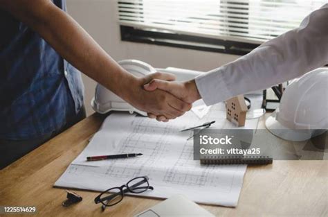 엔지니어 인테리어 디자이너 및 건축가가 인사말 인사를 건네며 건설 현장의 회의실 사무실 파트너십 계약자 개념에서 책상 위에 청사진이 있는 새로운 프로젝트 계약을 계획합니다