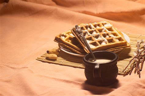 벨기에 와플은 발효 구운 우유 한 잔과 버드 나무 가지와 브라질 너트가있는 분홍색 식탁보에 복고풍 숟가락으로 대나무 매트 위에