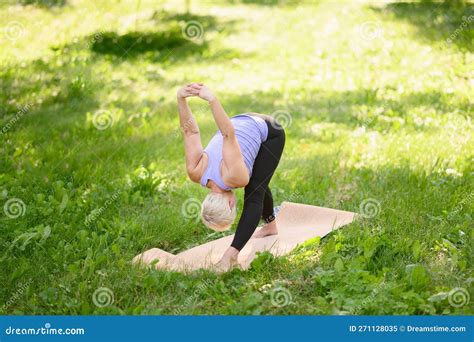 A Middle Aged Woman Practices Yoga Outdoors In The Standing Forward