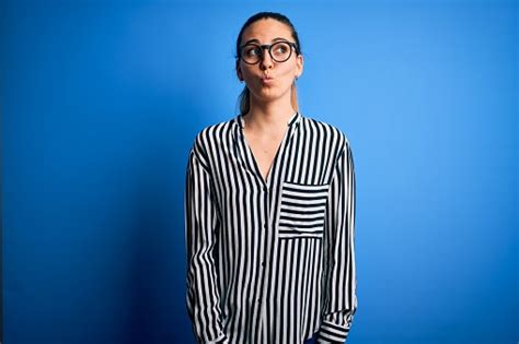 입술 미친 코믹 제스처와 물고기 얼굴을 만드는 파란색 배경에 줄무늬 셔츠와 안경을 입고 푸른 눈을 가진 아름다운 금발 여자 재미있는 표현 귀여운에 대한 스톡 사진 및 기타