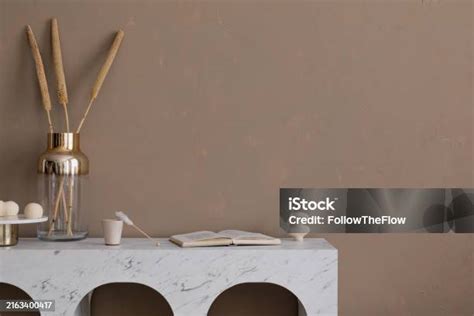 복사 공간 대리석 콘솔 책 금색 및 유리 꽃병 베이지 색 조각품 갈색 벽 및 개인 액세서리가있는 따뜻한 거실 인테리어의 미니멀리즘 구성 가정 장식 템플렛 0명에 대한 스톡