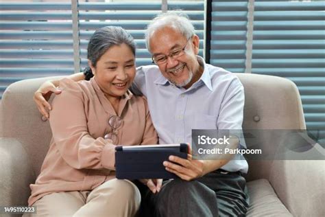 행복한 미소를 짓고 있는 아시아 노부부는 소파에 앉아 태블릿을 사용하며 집 거실에서 친구나 친척 사촌과 온라인 화상 통화를 한다 인터넷 정보 기술과 라이프스타일 개념