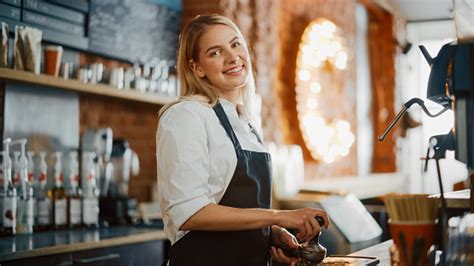 금발 머리를 가진 아름다운 젊은 백인 바리스타카페에서 신선한 커피 한 잔을 만들고 있습니다 아늑한 로프트 스타일의 커피 숍 레스토랑 카운터에서 일하는 동안 행복하고 웃는 바