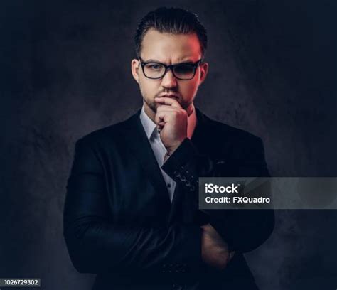 ภาพระยะใกล้ของนักธุรกิจที่มีสไตล์รอบคอบพร้อมใบหน้าที่จริงจังในชุดสูทและแว่นตาที่เป็นท ภาพสต็อก