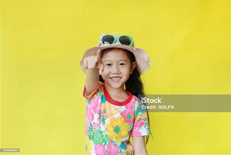 노란색 배경 위에 고립된 카메라를 가리키는 행복한 아시아 소녀 꽃무늬 여름 드레스와 모자를 쓰고 선글라스를 쓴 아이 휴일과 여름 패션 컨셉 4 5세에 대한 스톡 사진 및