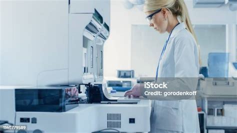 여성 연구 과학자 분석기 의료 기계에 혈액 샘플을 가진 테스트 튜브를 퍼 팅 과학자는 제약 실험실에서 현대 의료 장비와 함께 작동 합니다 기계류에 대한 스톡 사진 및 기타