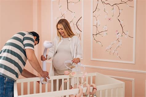 쾌활한 부모는 아기 방을 꾸미고 유아용 침대를 조립하고 유아용 침대 위에 매달린 장난감을 놓습니다 2명에 대한 스톡 사진 및 기타 이미지 Istock