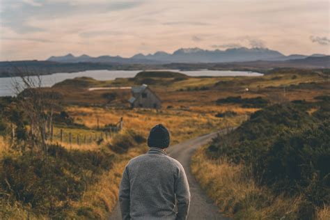 회색 재킷과 모자를 쓴 남자가 하얗고 회색 하늘 아래 도로 전망 필드와 수역에 서 있습니다 사진 Unsplash의 무료 사람의 이미지